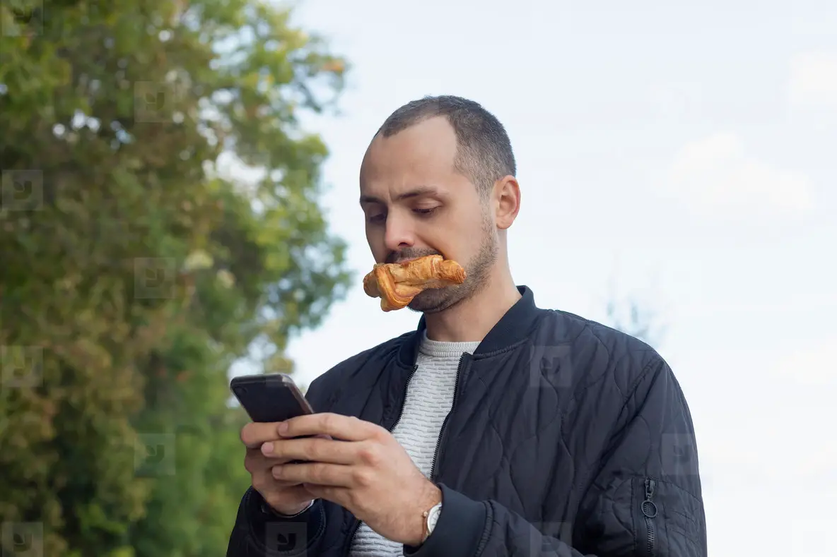 Young Man Eating And Using Smart Phone Photo (224391) - YouWorkForThem