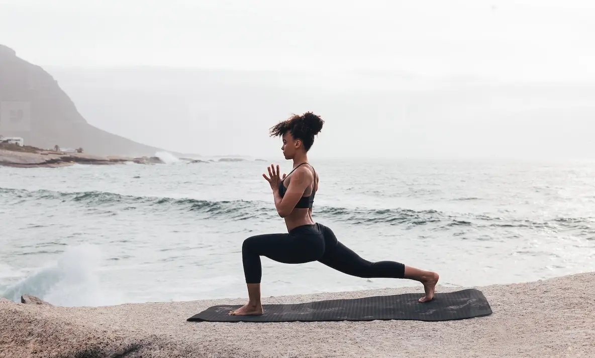 Side View Of Female Practicing Yoga On A Mat By The Ocean In The ...