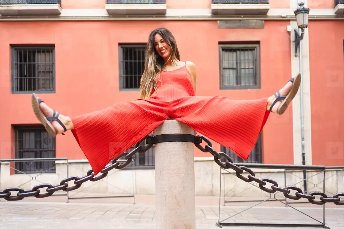 A Woman In A Vibrant Red Dress Poses Playfully On A Chain Barrier, Radiating Confidence Photo ...